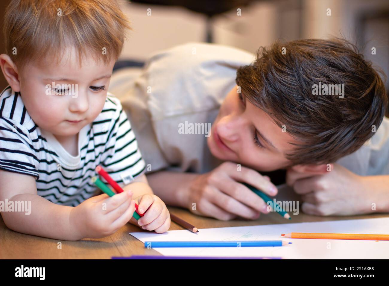 Two children draw with colored pencils. A teenager and a younger ...