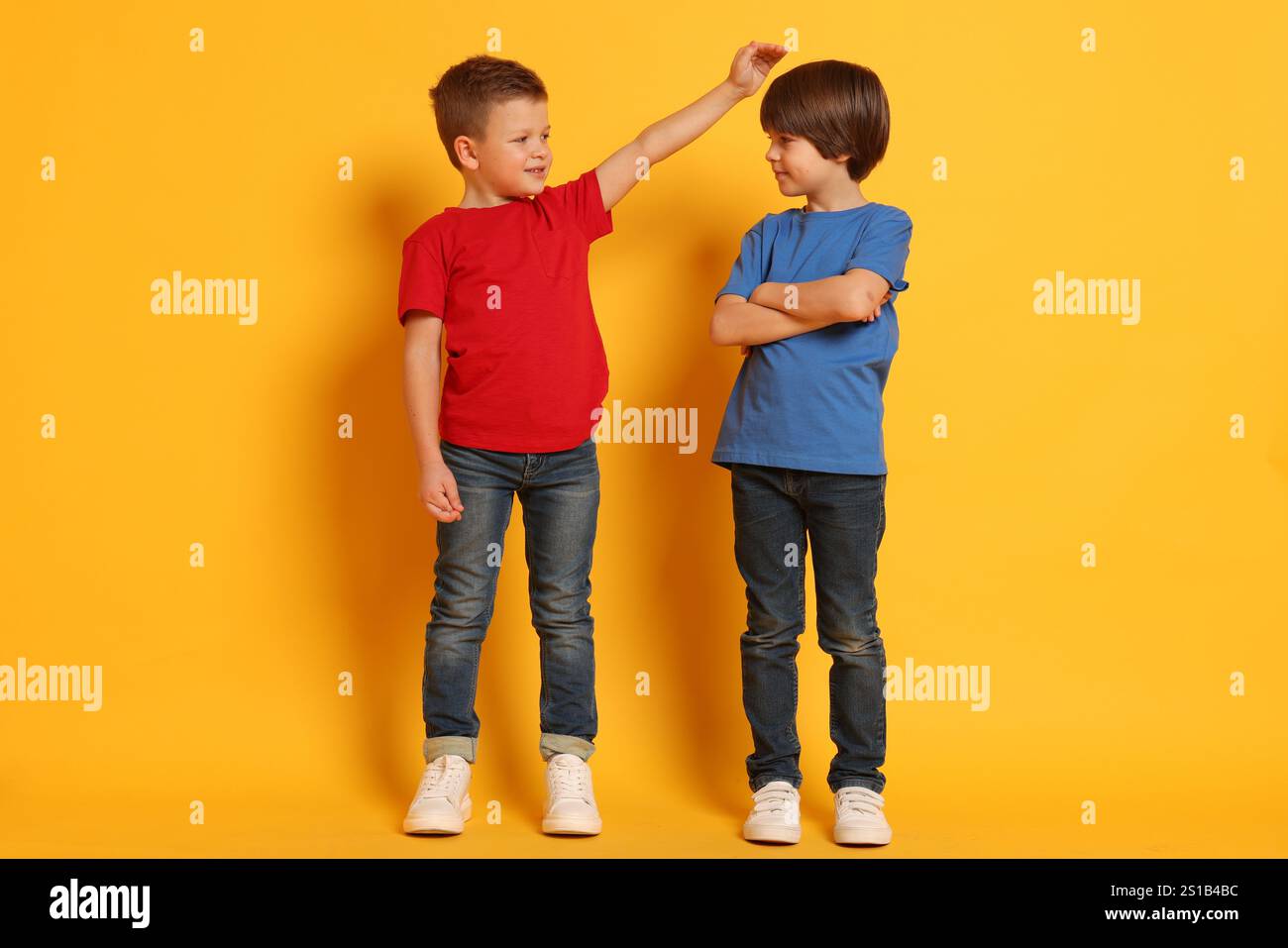 Cute brothers comparing their height on orange background Stock Photo ...