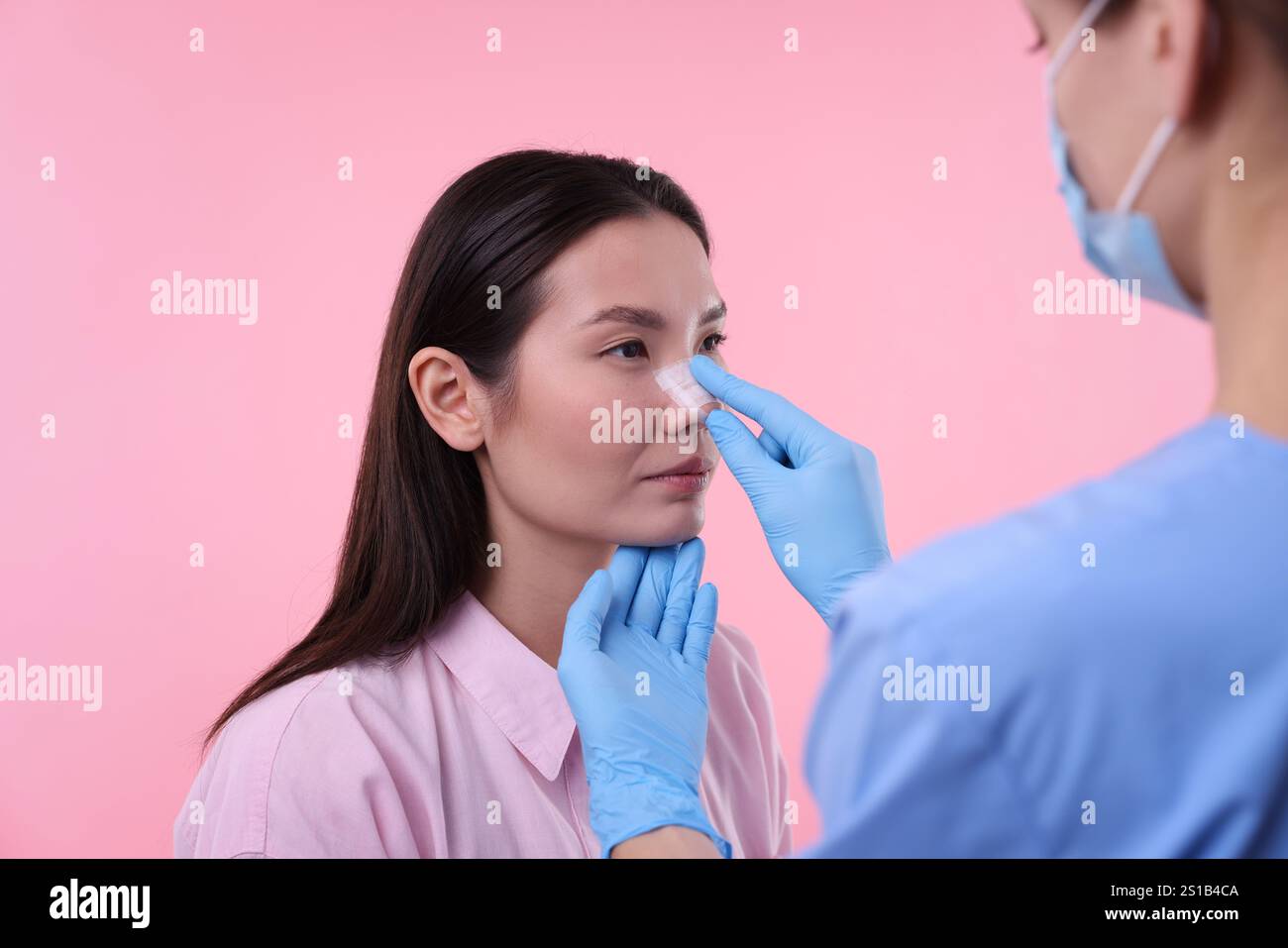 Doctor checking patient's nose after plastic surgery operation on pink ...