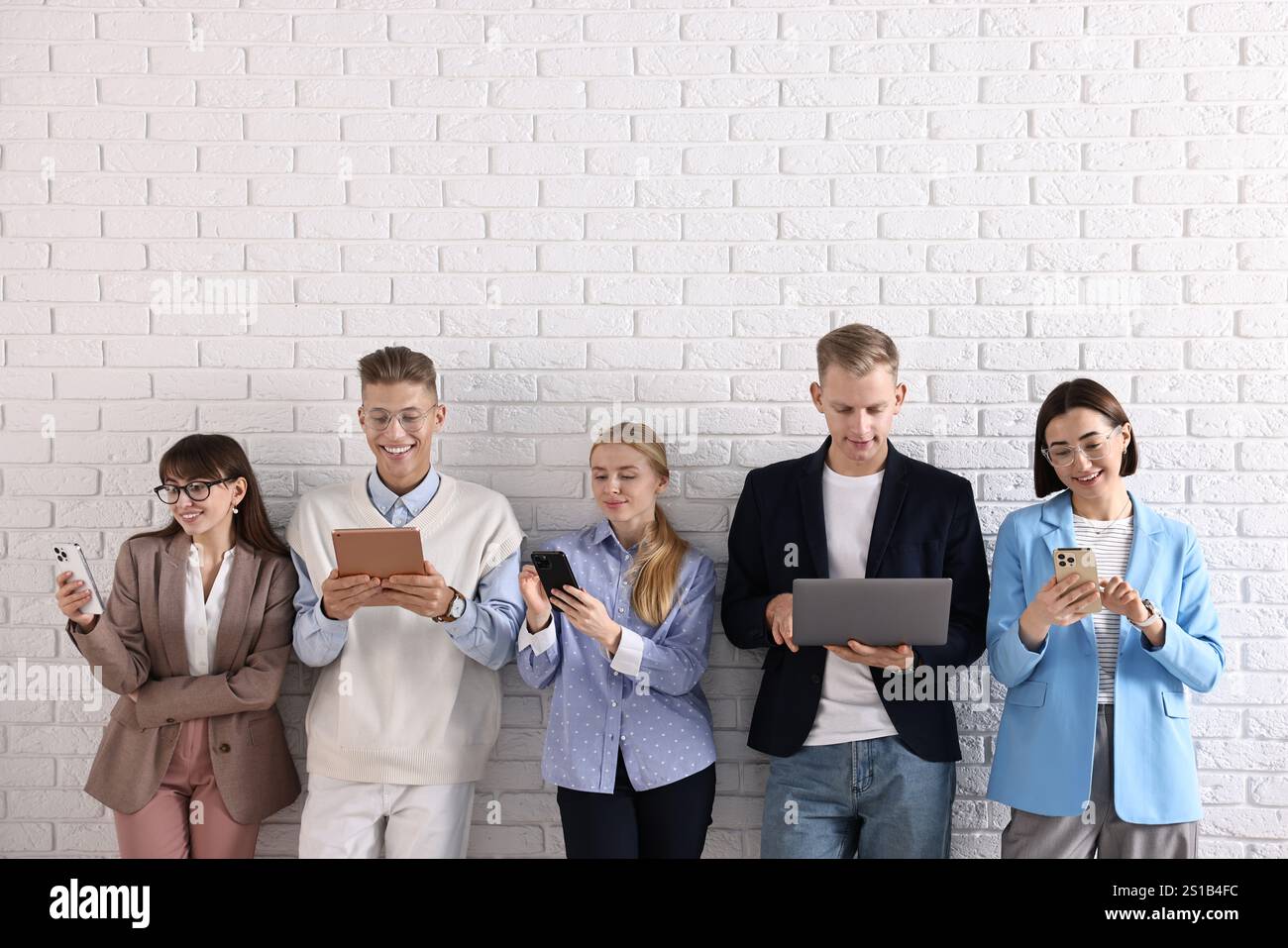 Group of people using different gadgets near white brick wall indoors ...
