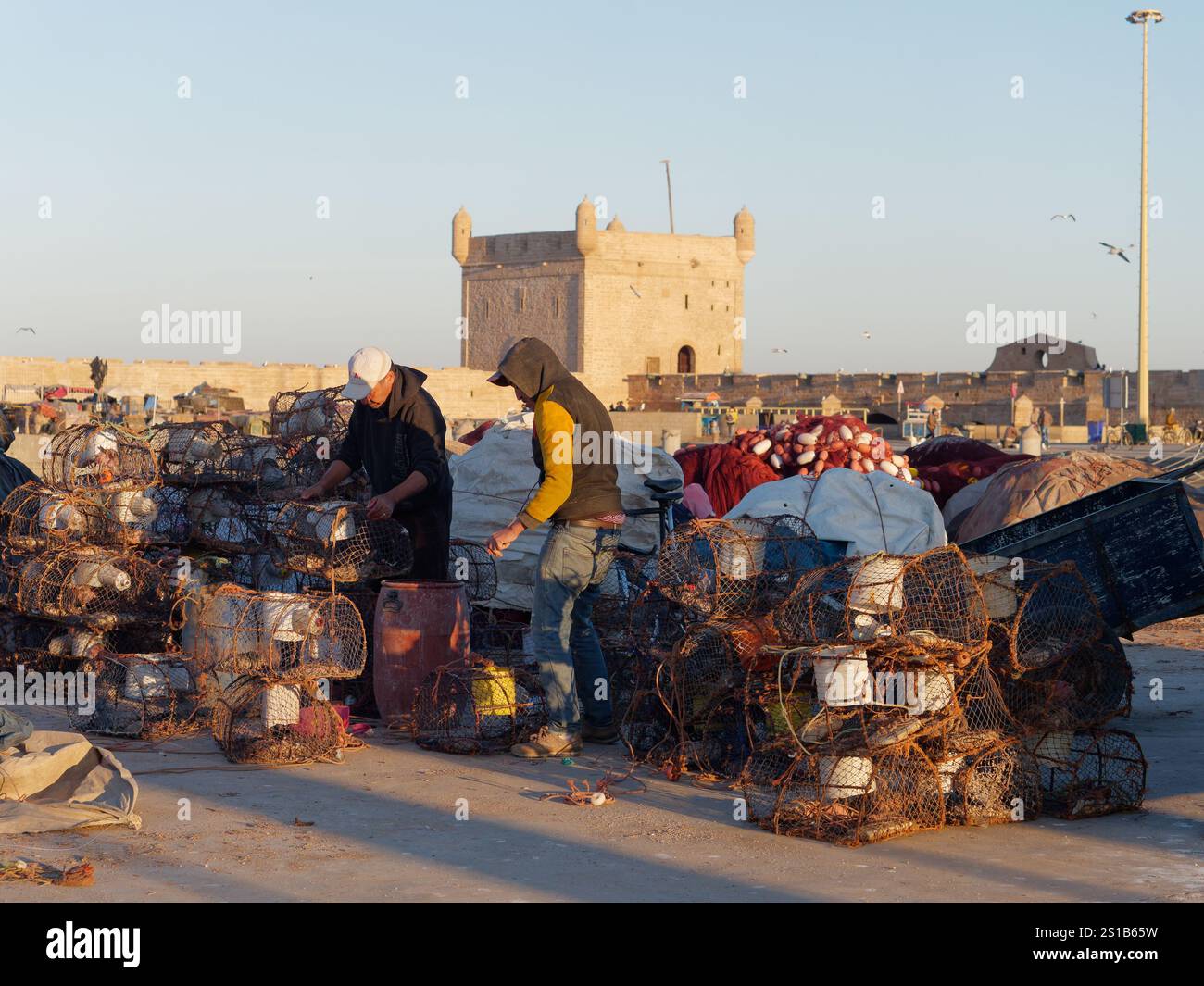 Men attend to fishing nets in the fishing port with tower of fort ...