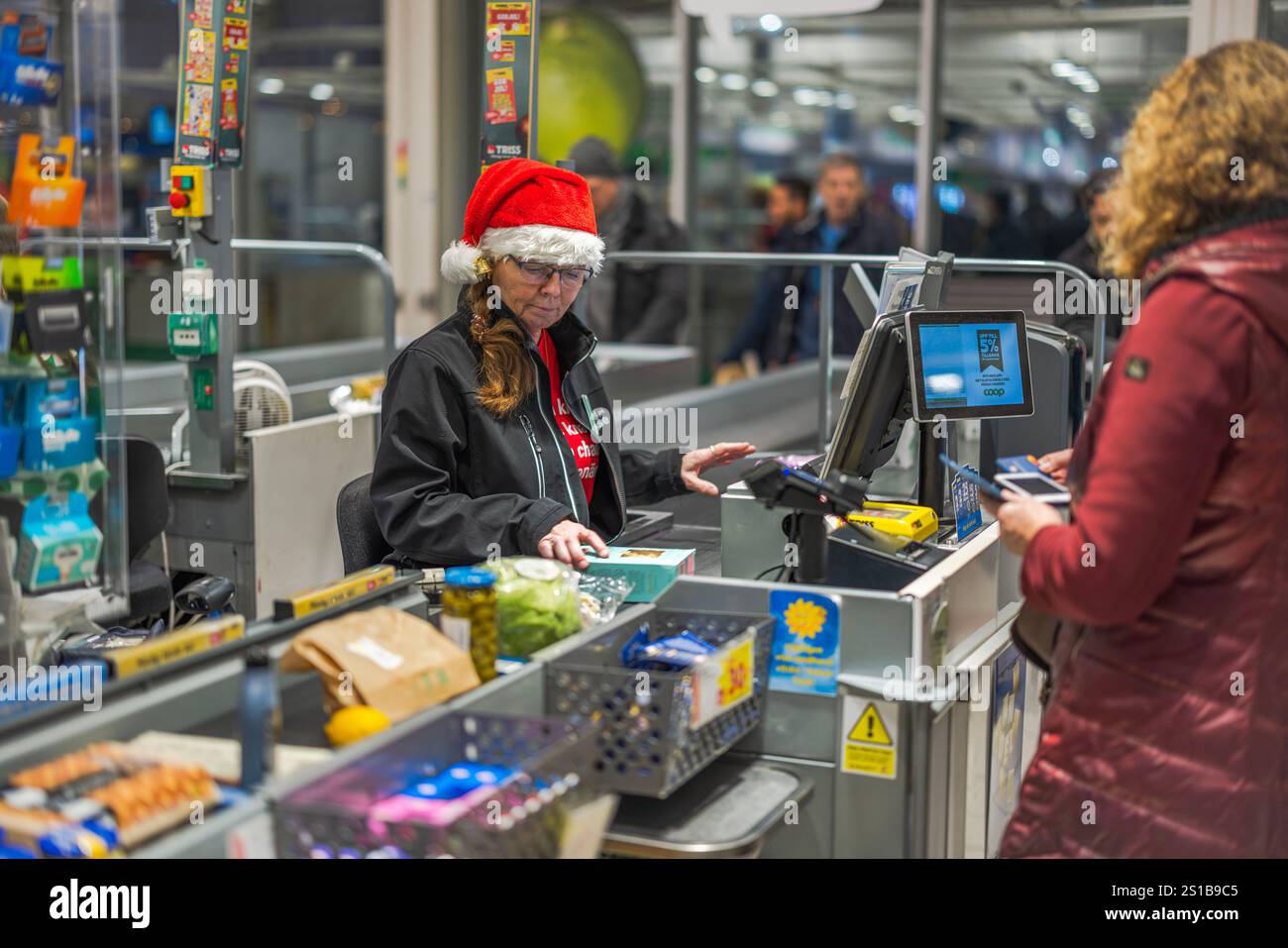 Cashier wearing Santa hat scanning groceries at supermarket checkout ...