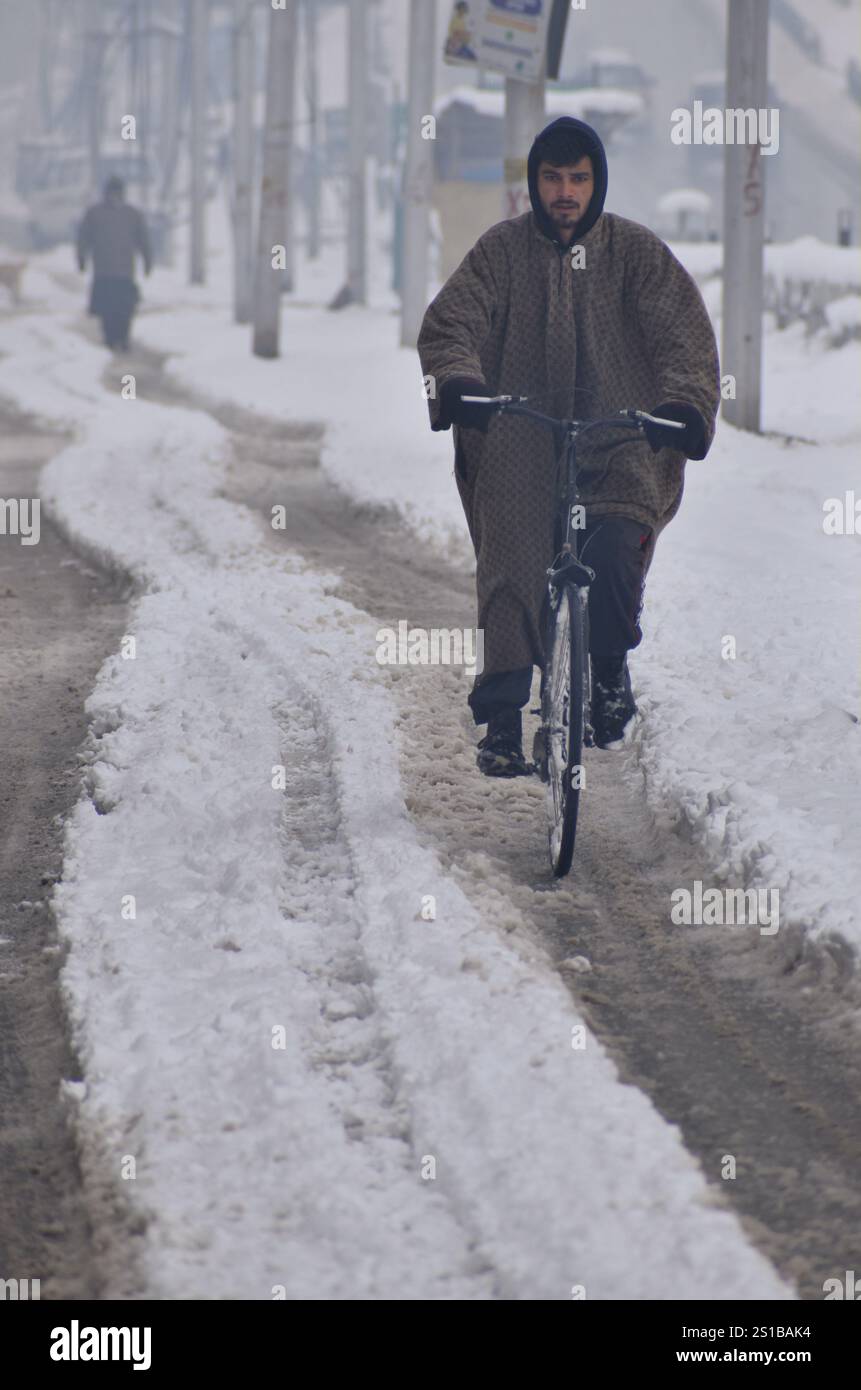 Srinagar, India. 28th Dec, 2024. A person riding a bicycle on a snow ...