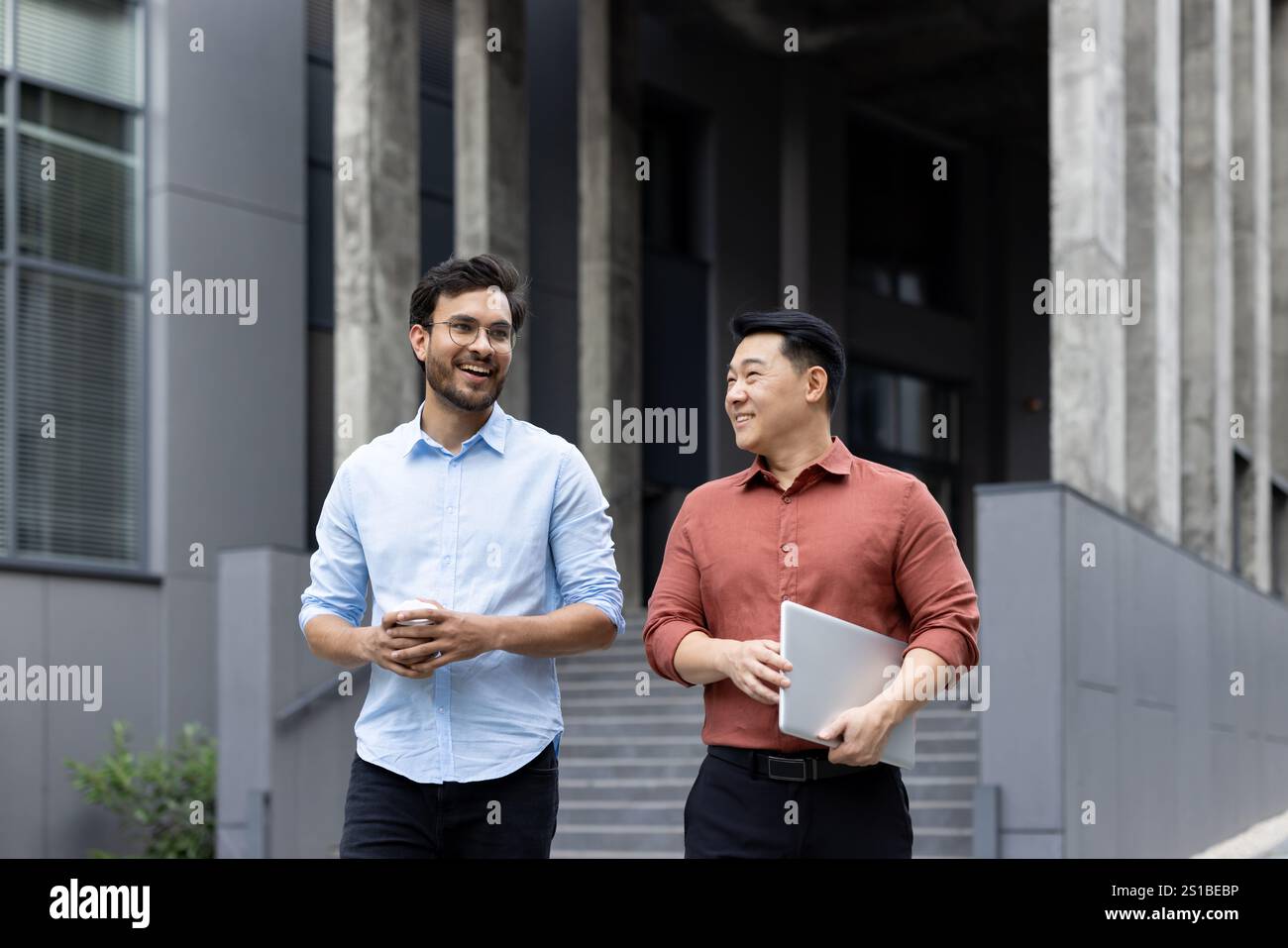 Two men walking and chatting outside an office building, colleagues and ...