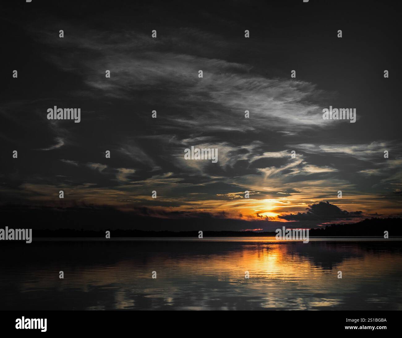 A mesmerizing sunset over a peaceful lake, featuring dramatic clouds ...