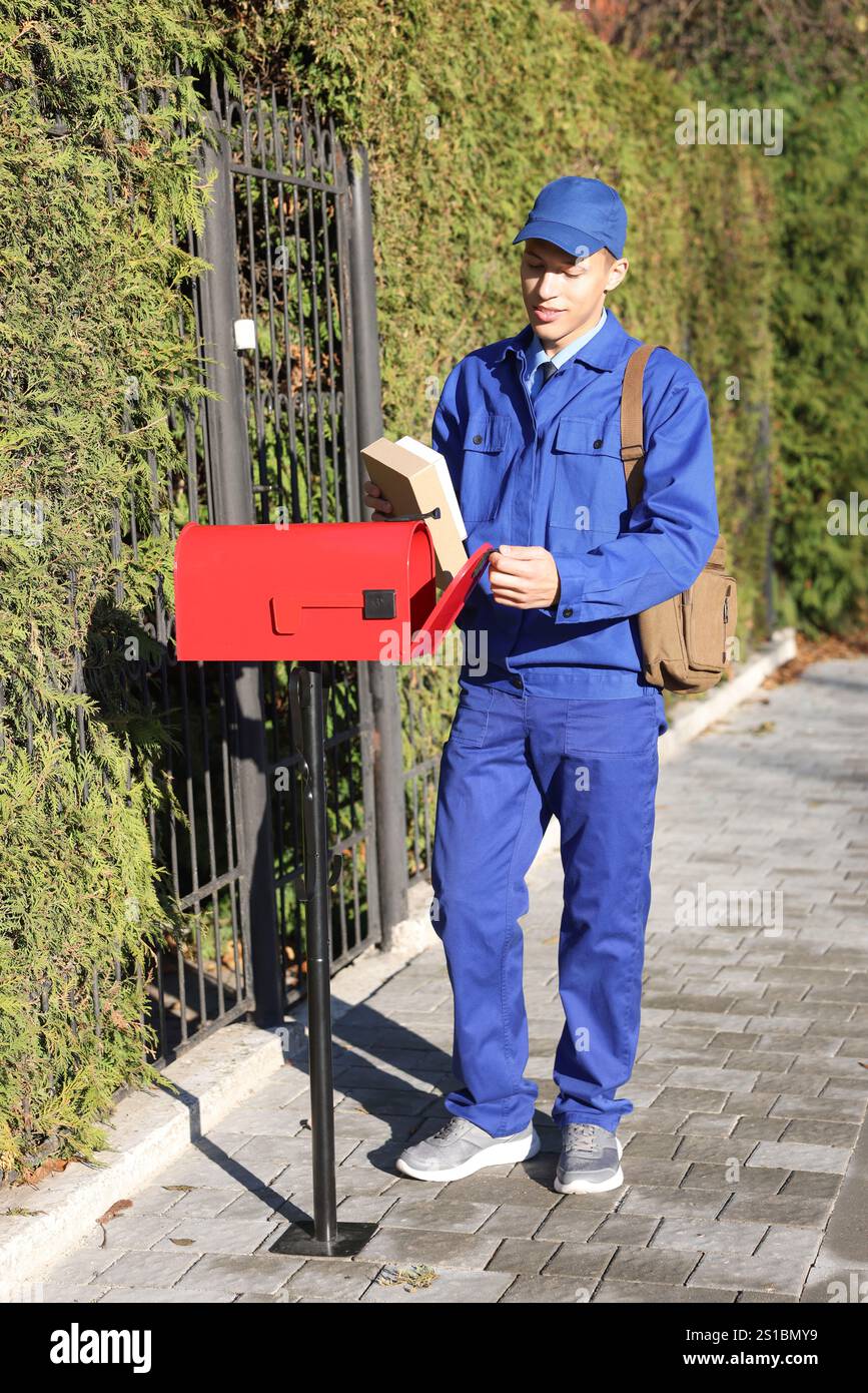 Postman putting parcel into mail box outdoors Stock Photo - Alamy