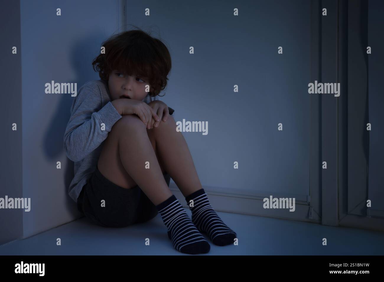 Fearful boy hiding on windowsill at night. Space for text Stock Photo ...