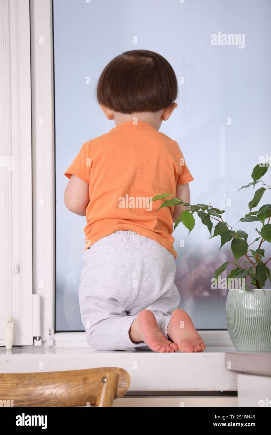 Little boy near window on windowsill, back view. Dangerous situation ...