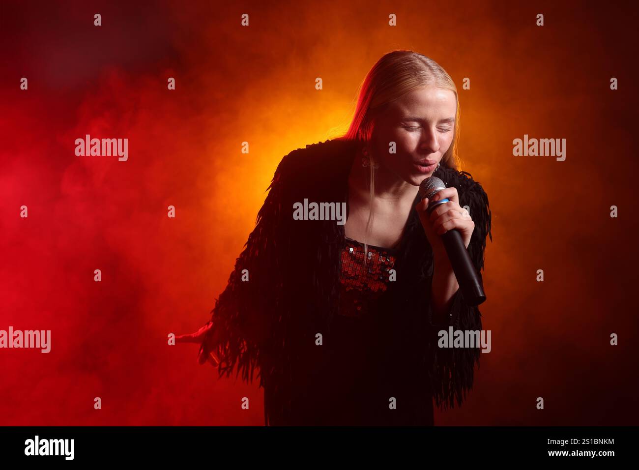 Beautiful singer performing on dark background with red light and smoke ...