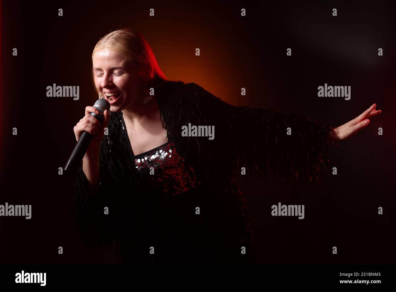 Beautiful singer performing on dark background with orange light Stock ...