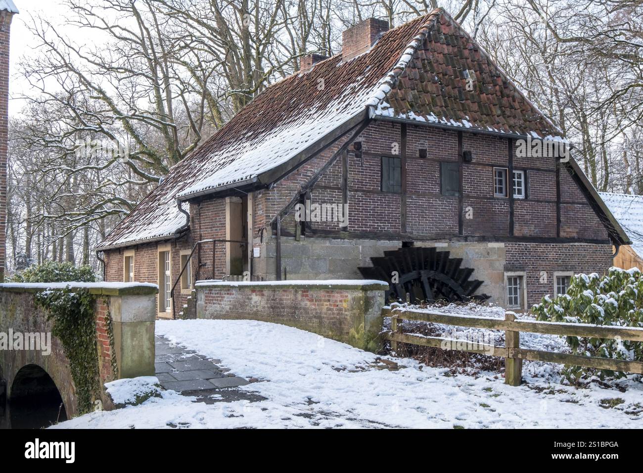 Watermill with stone bridge and red roof tiles in winter with snow ...