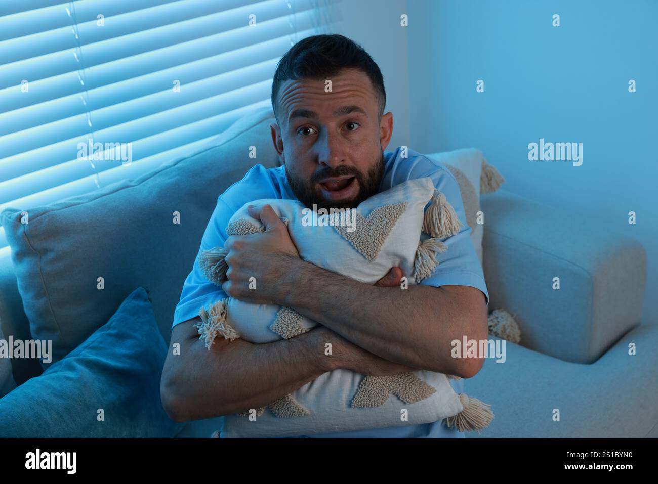Fear of darkness. Scared man hugging pillow on couch in dark room Stock ...