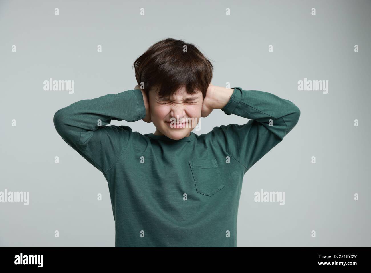 Annoyed boy covering his ears due to loud sound on grey background ...