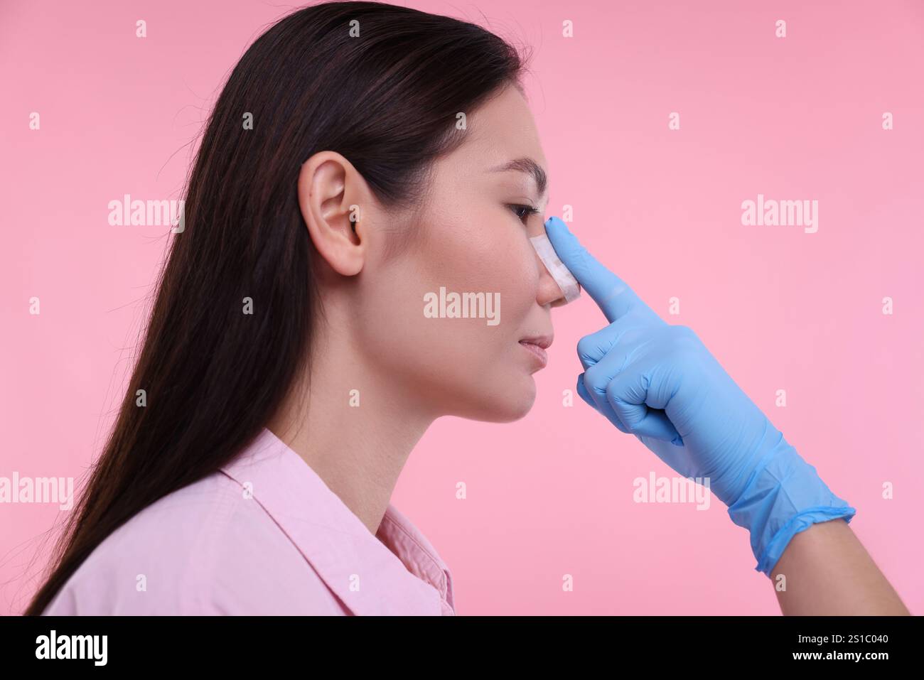 Doctor checking patient's nose after plastic surgery operation on pink ...