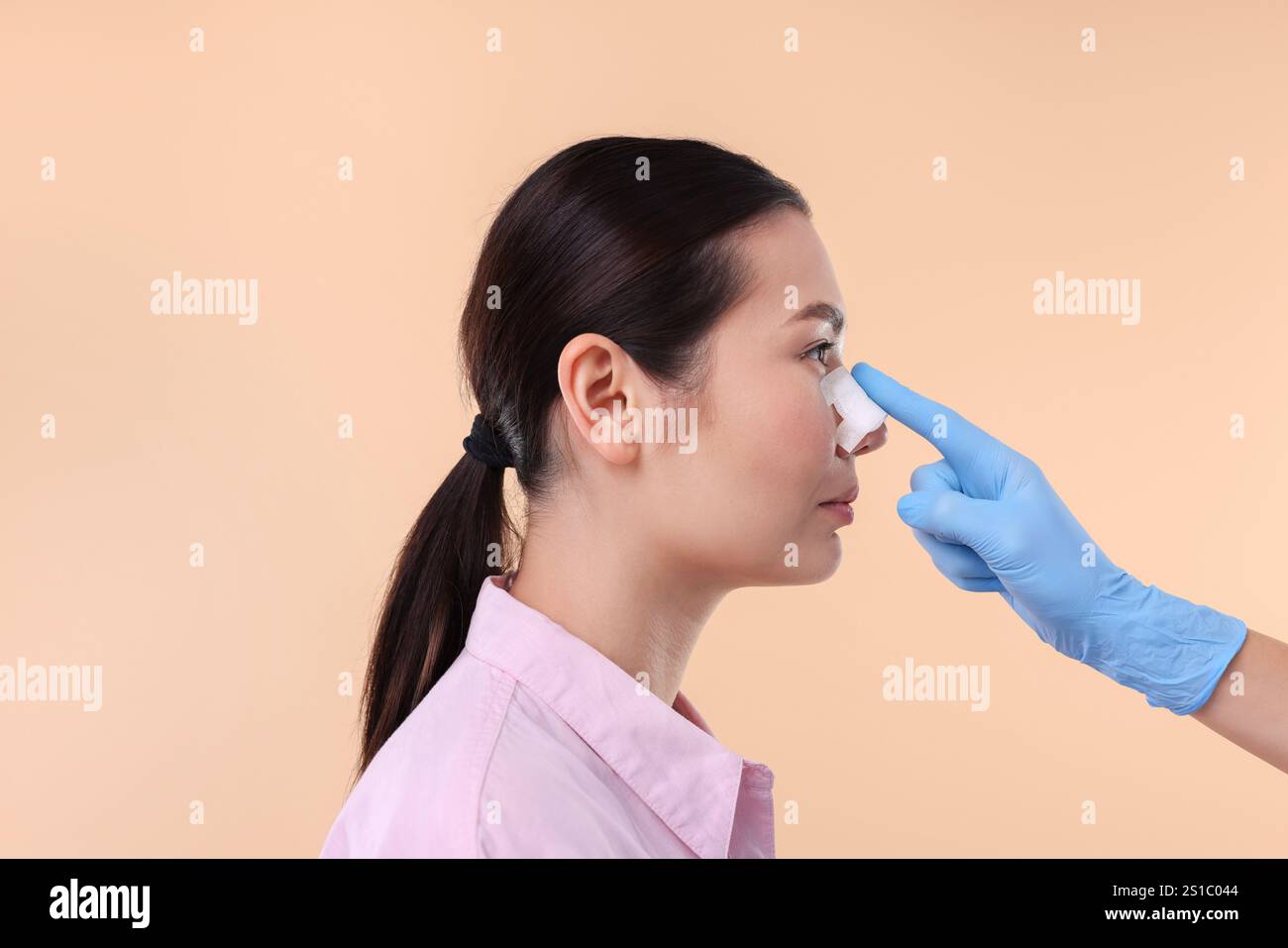 Doctor checking patient's nose after plastic surgery operation on beige ...