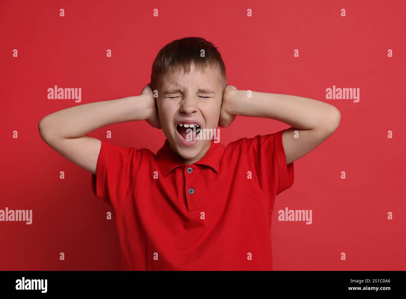 Little boy covering his ears on red background Stock Photo - Alamy
