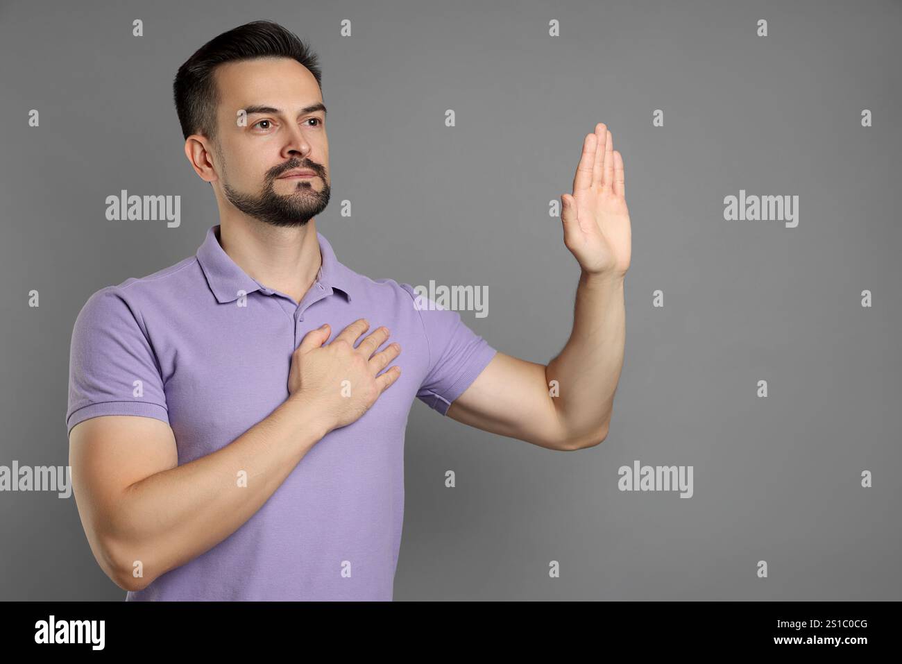 Man making promise with raised hand on grey background, space for text ...