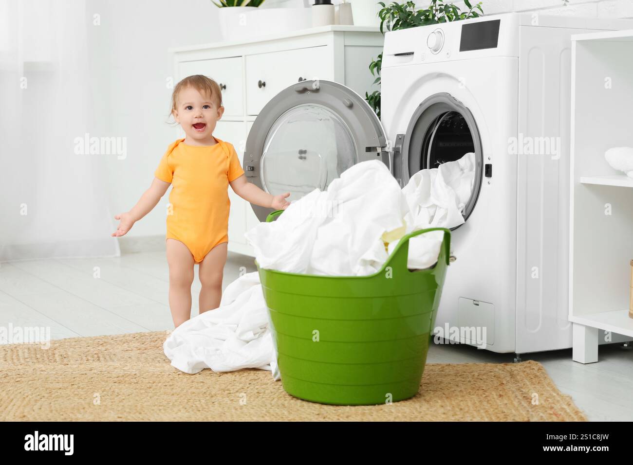 Cute little baby doing laundry in bathroom Stock Photo - Alamy