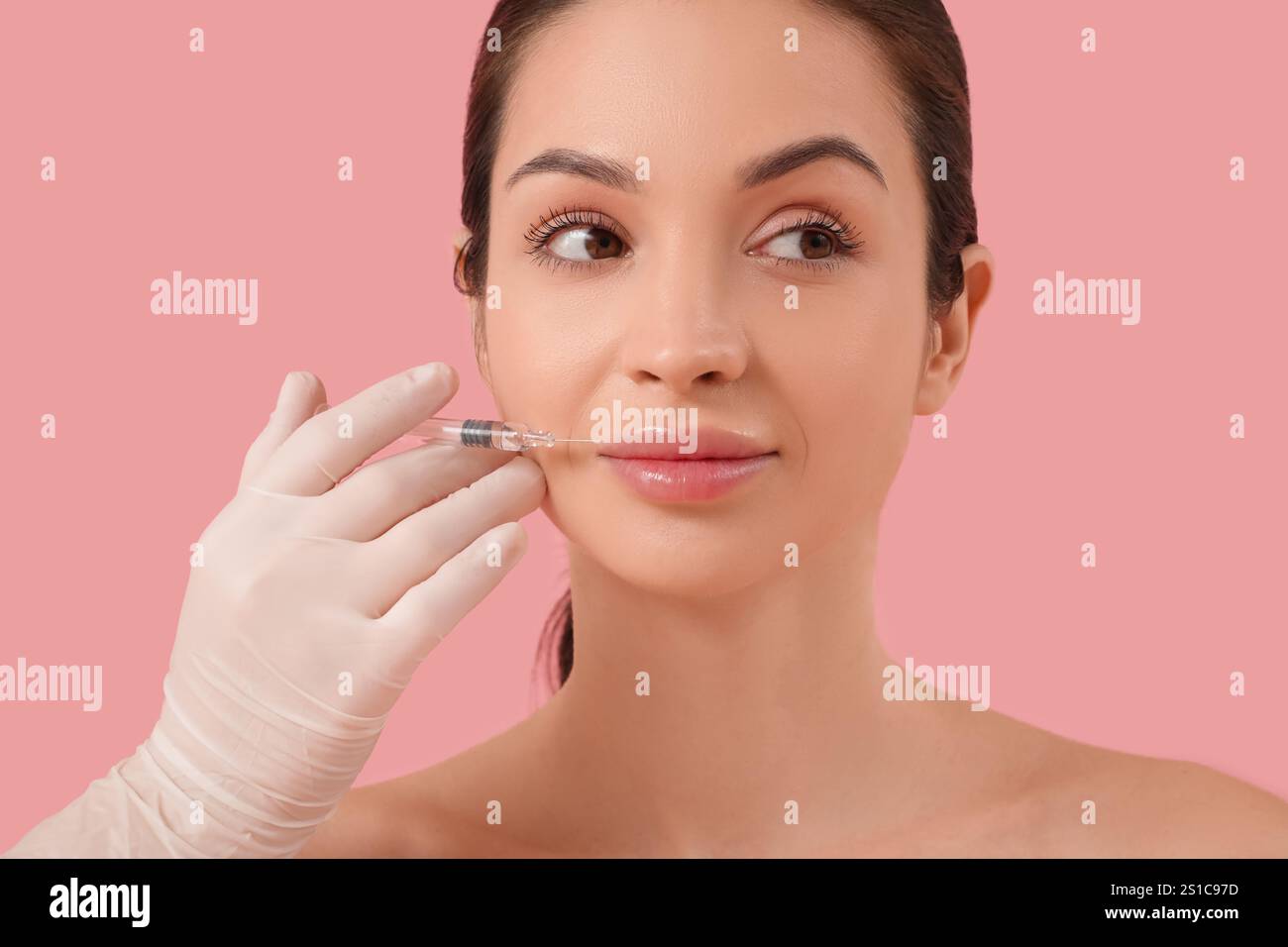 Beautiful young happy woman receiving lips injection on pink background ...