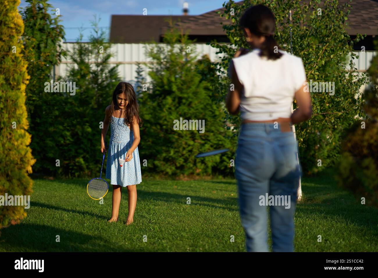 Child playing badminton in a sunny backyard with parent in the ...
