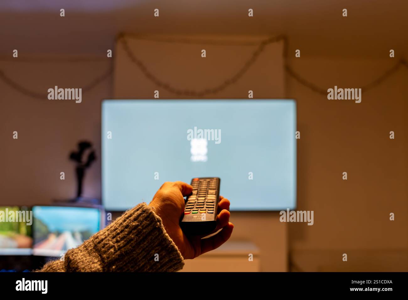 Hand holding tv remote control changing channels pointing to large flat ...