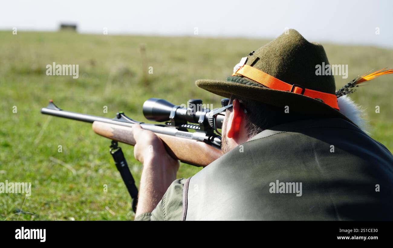 Hunter in camouflage aims his rifle in a dense forest, blending with ...