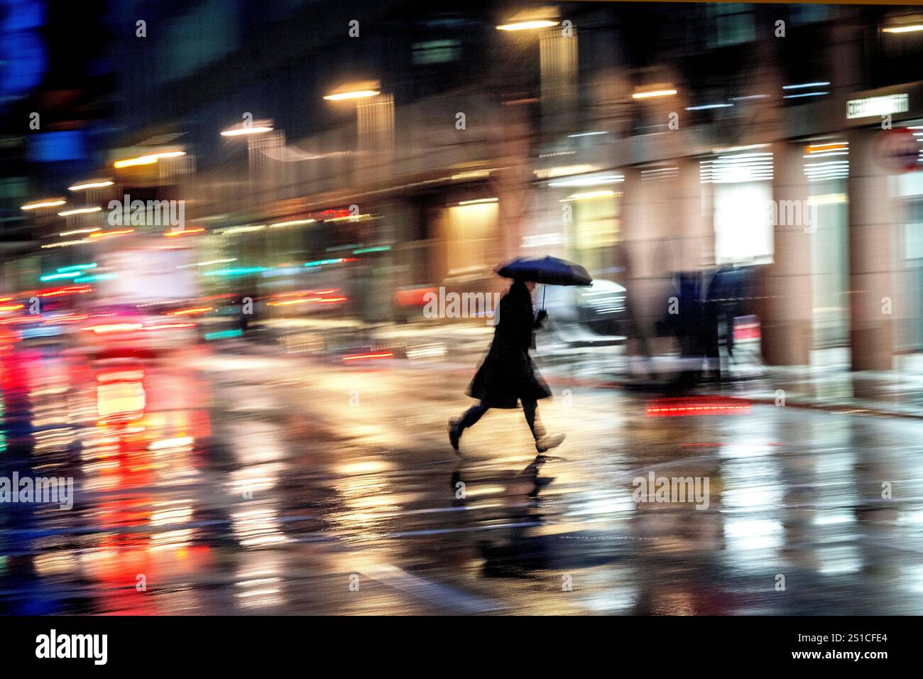 A man crosses the street on a rainy and windy day in Frankfurt, Germany ...