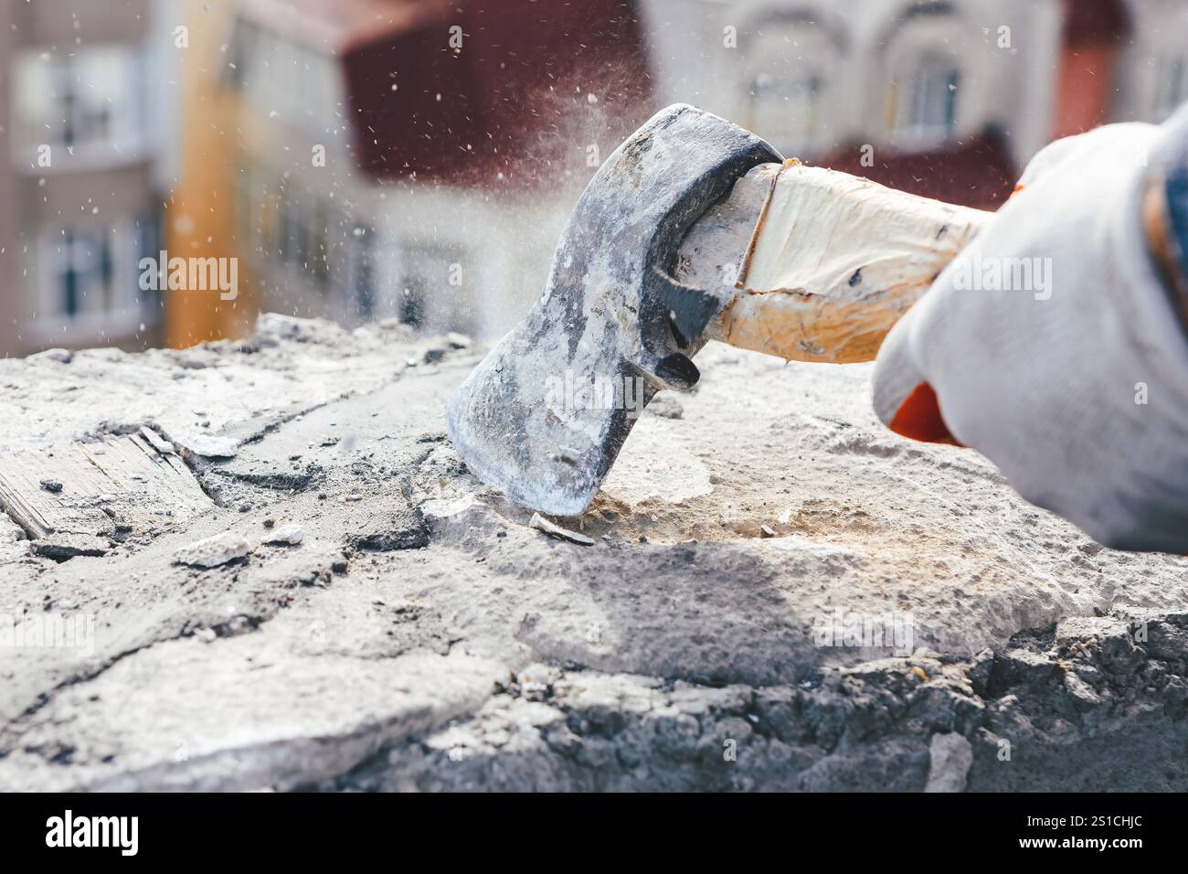 Worker breaking concrete with a metal hammer, wearing protective gloves ...