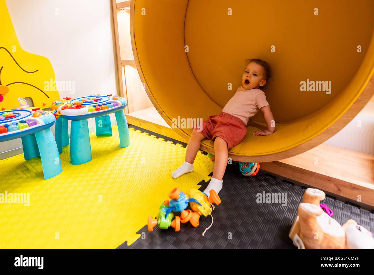 Happy child sitting inside a round yellow play structure in a colorful ...