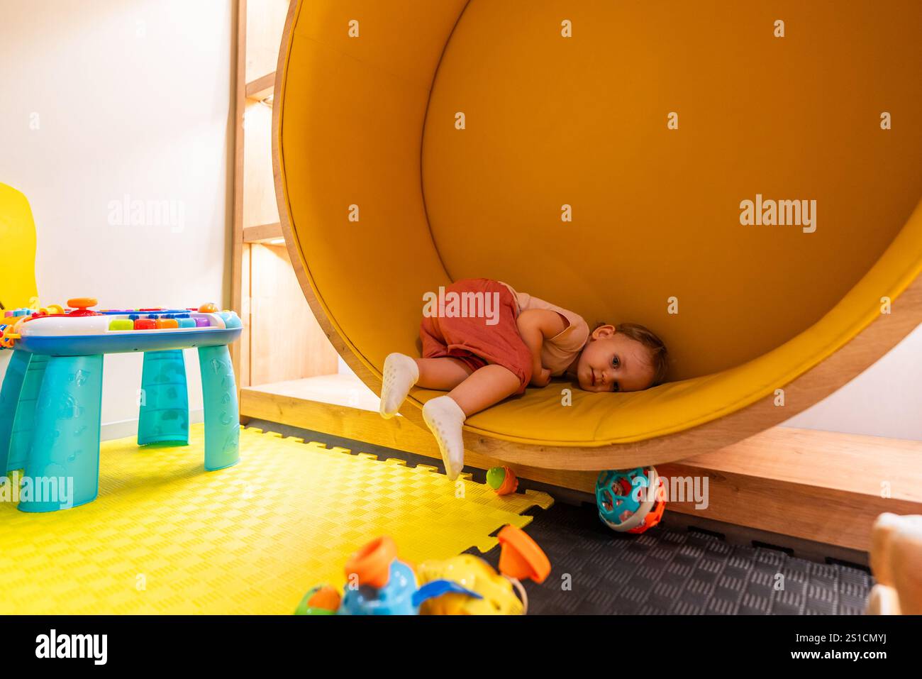 Young child lying down inside a round yellow play nook in a vibrant ...