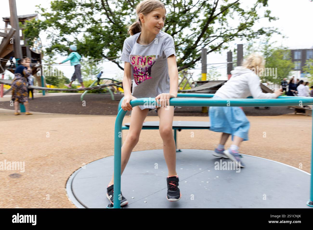 An 8 year old white girl spins on a roundabout in a playground at Brent ...