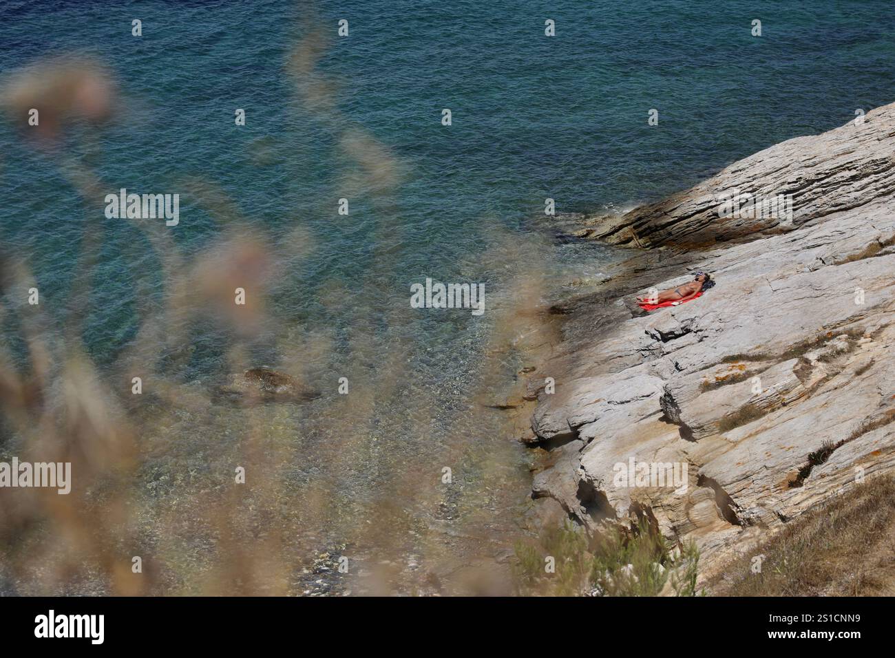 A woman is sunbathing on rocks on the island of Porquerolles, in Port ...