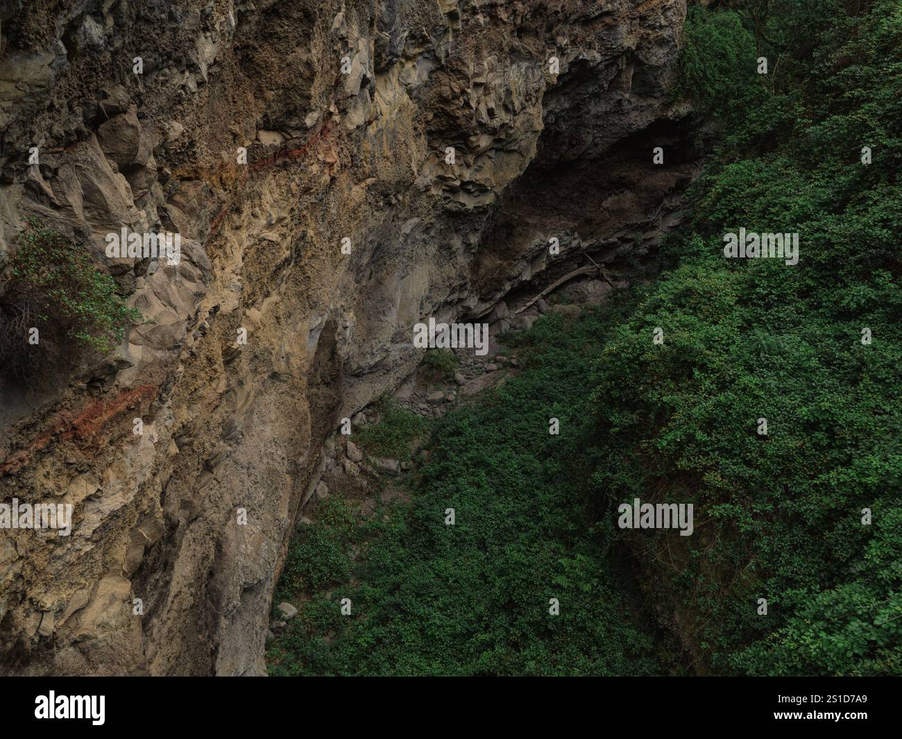 A rugged cliff with weathered rock layers and red streaks on the left ...