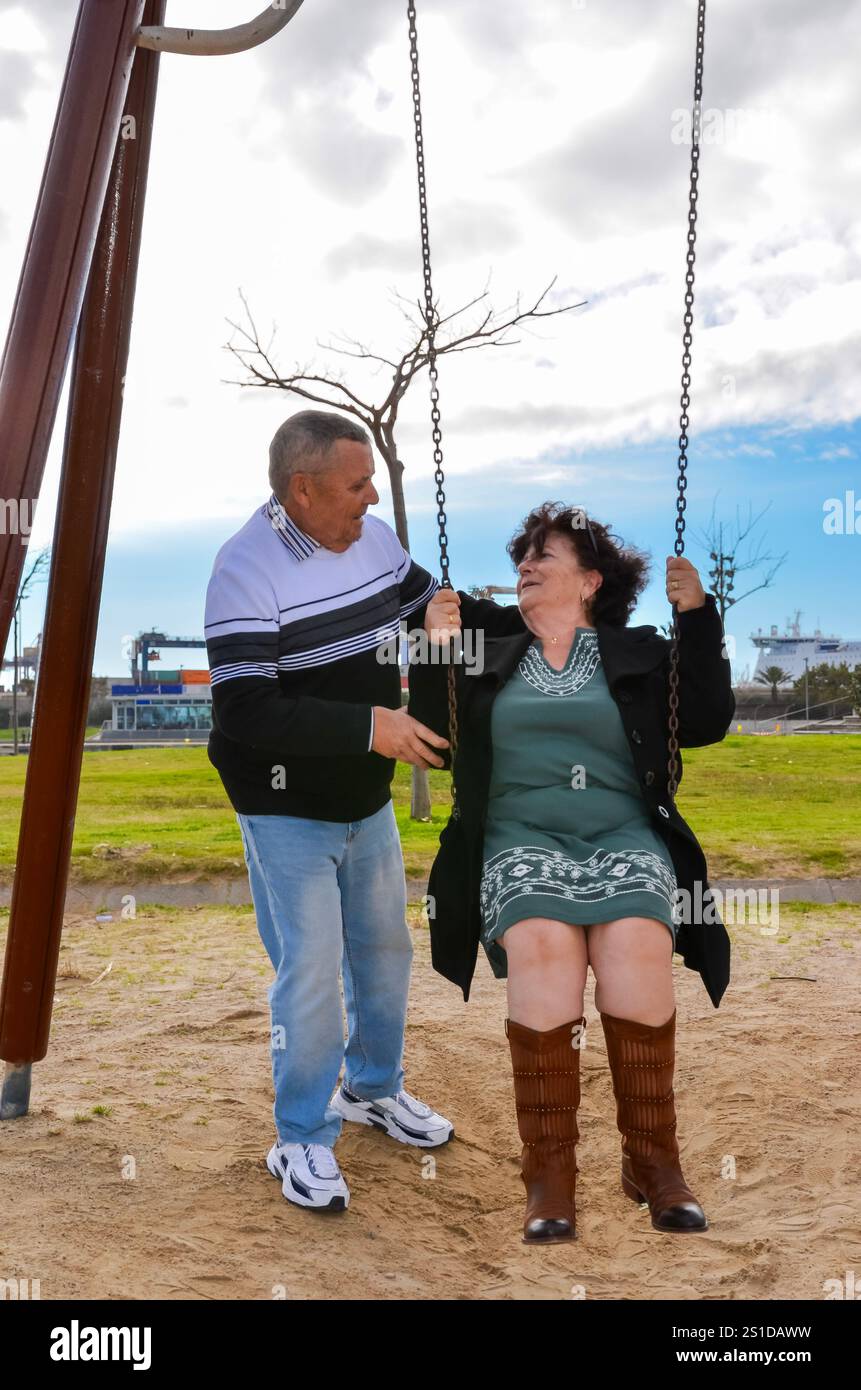Senior man pushing senior woman on a swing in a playground Stock Photo ...