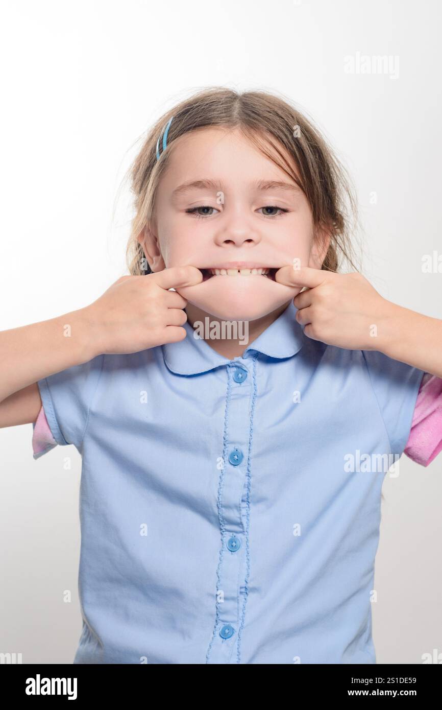 A young girl with brown hair makes a silly face, pulling her lips and ...