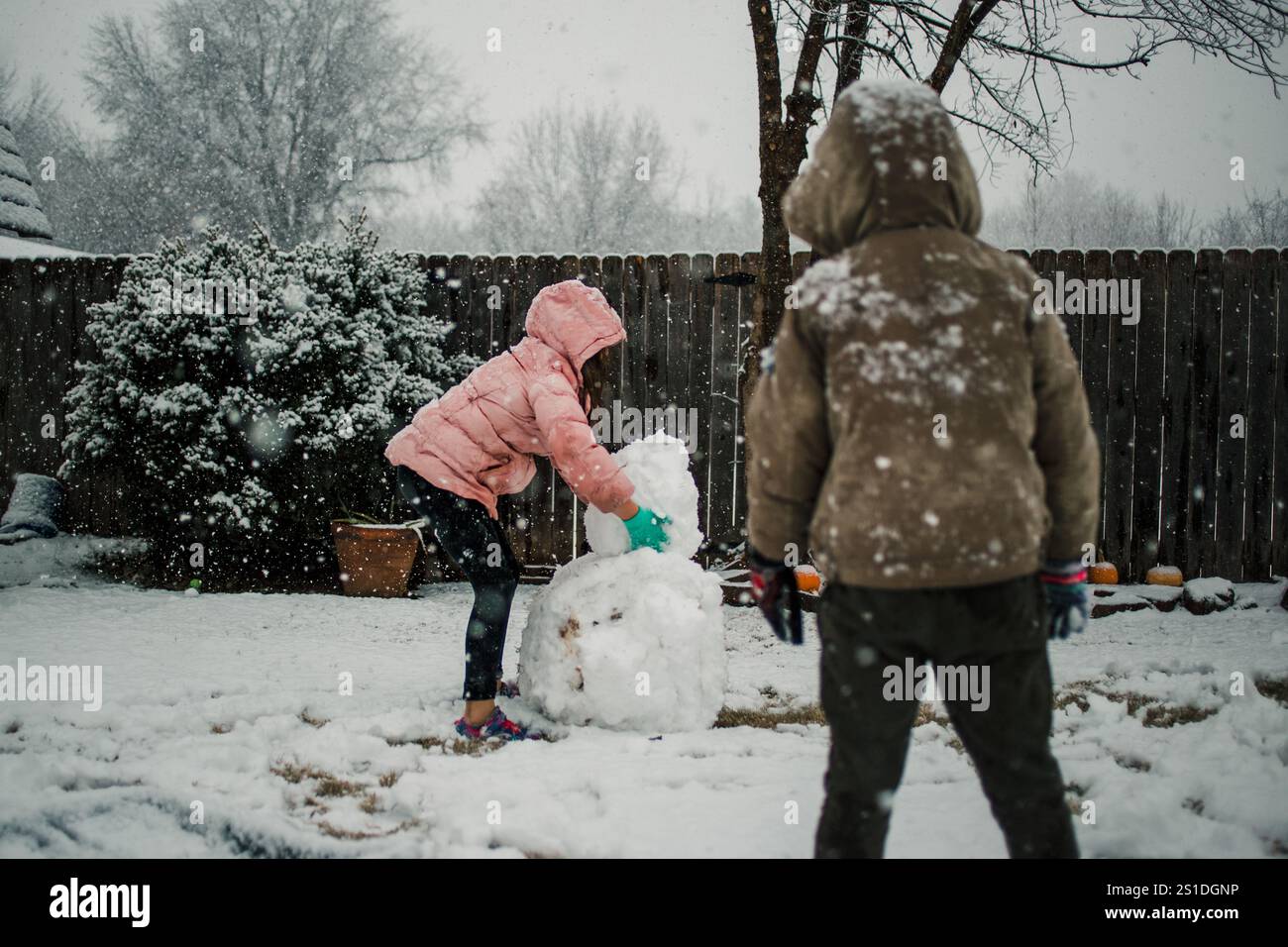 Two kids building a snowman in backyard Stock Photo - Alamy