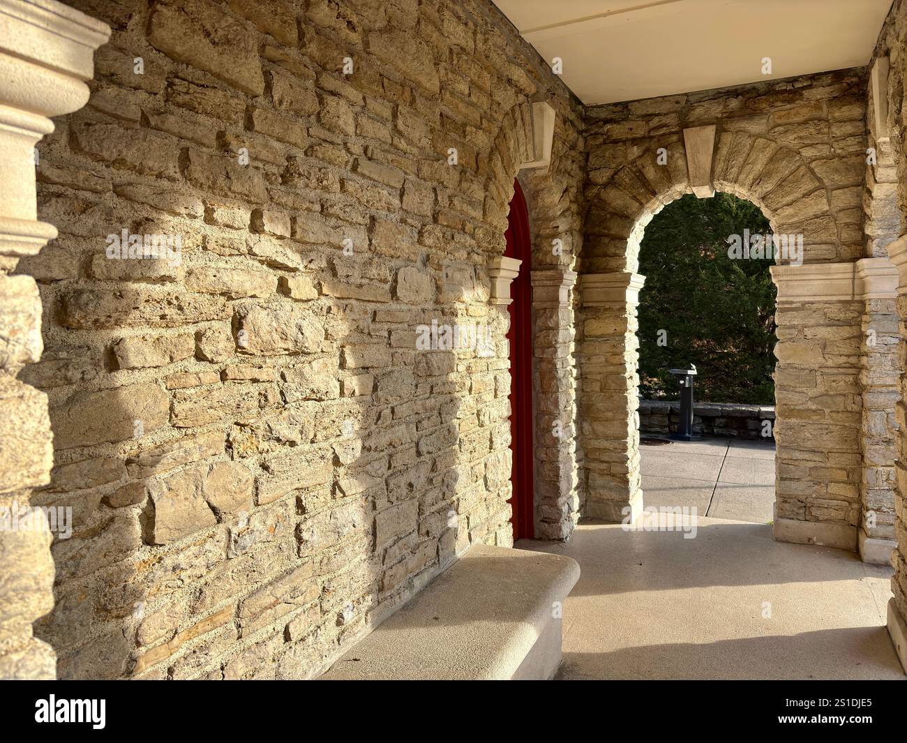 Sunlit stone corridor with arched entrances, textured walls Stock Photo ...