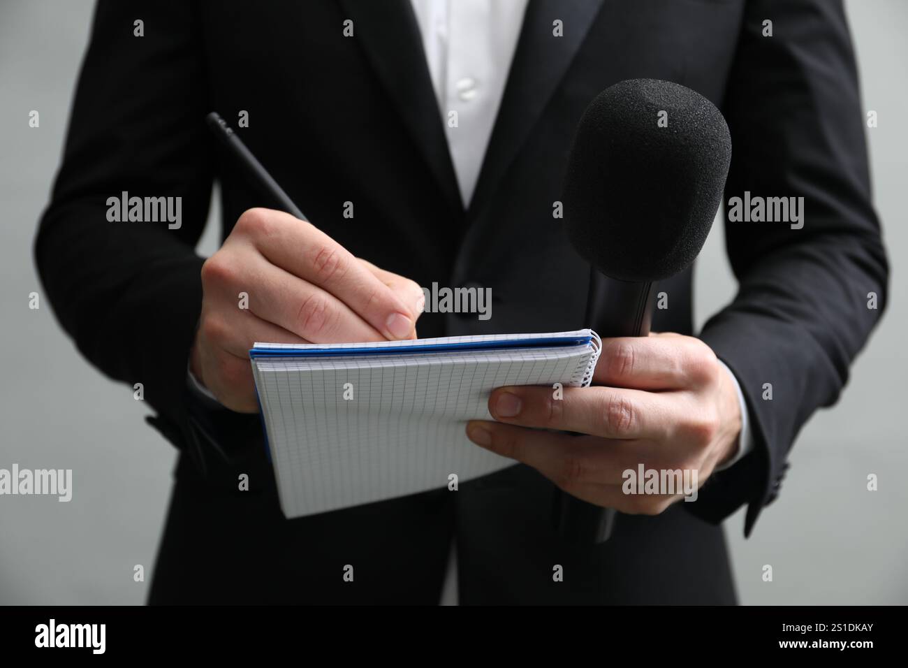 Journalist with microphone taking notes on grey background, closeup ...