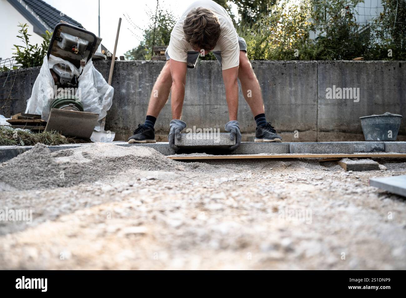 A construction worker carefully places a concrete paver on a prepared ...