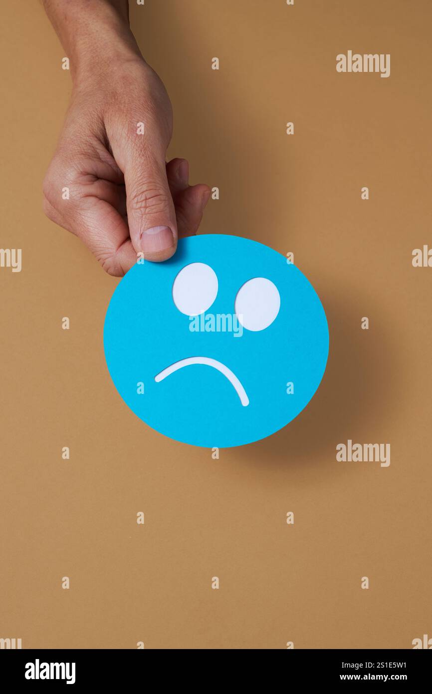closeup of a man with a blue sad face in his hand on a brown background ...