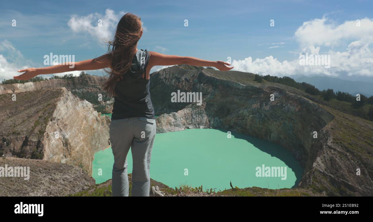 A woman stands confidently on the summit of a mountain overlooking a ...