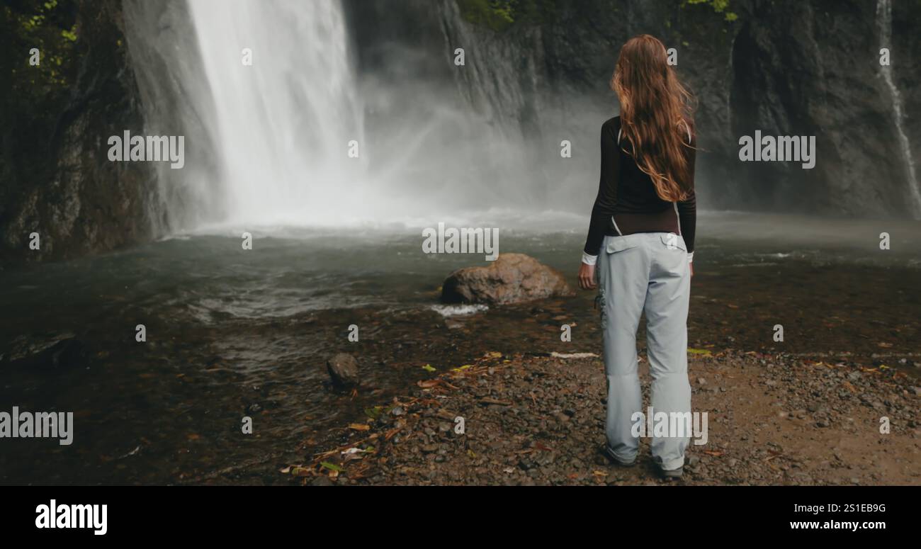 Female hiker is admiring a powerful waterfall cascading down a rocky ...