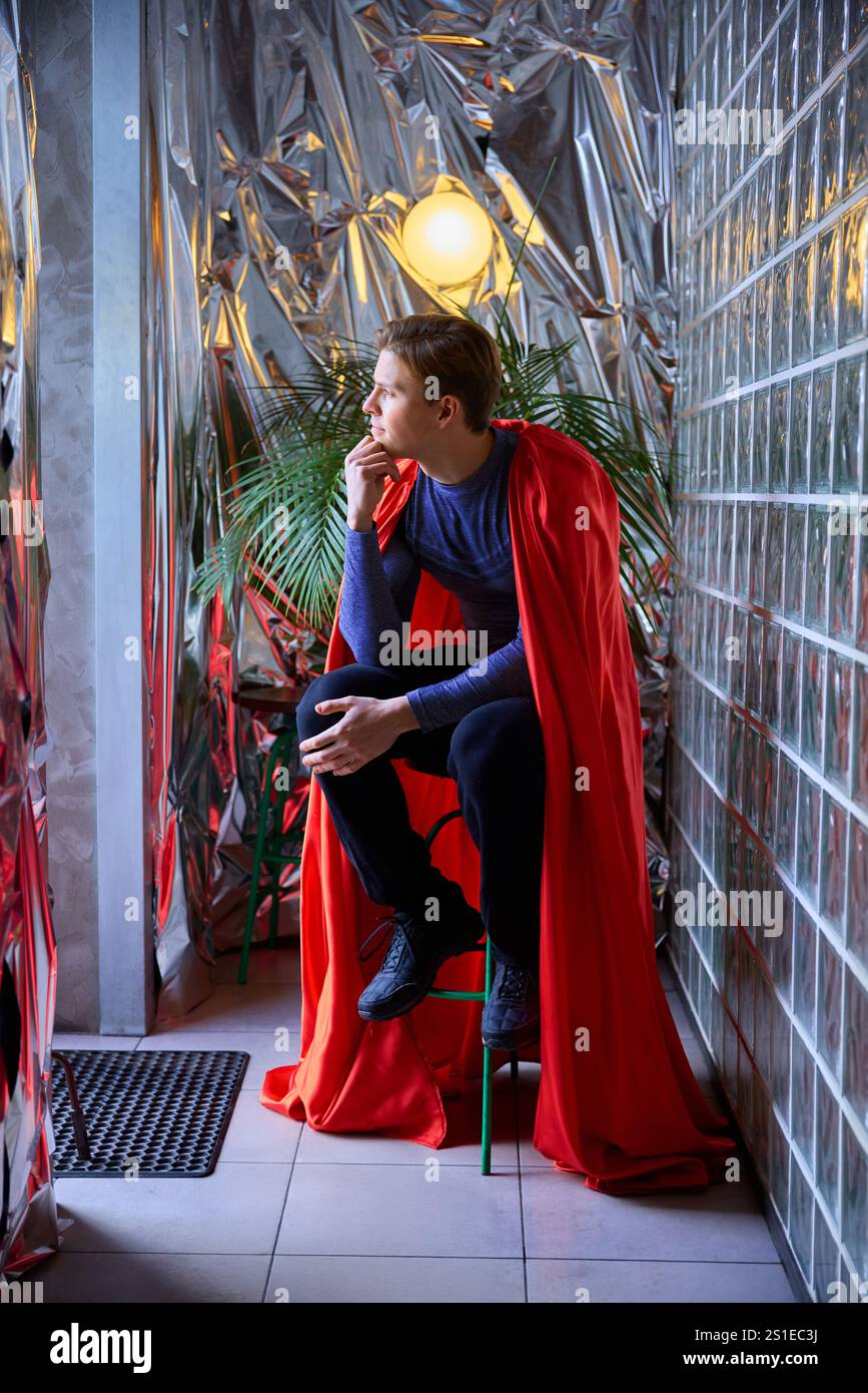 Superhero-dressed man sits by metallic wall, thoughtful gaze reflecting inner strength ...