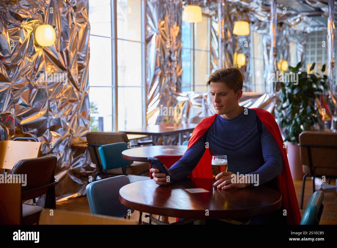 Man in cape holds phone, multitasking with beer, representing modern ...