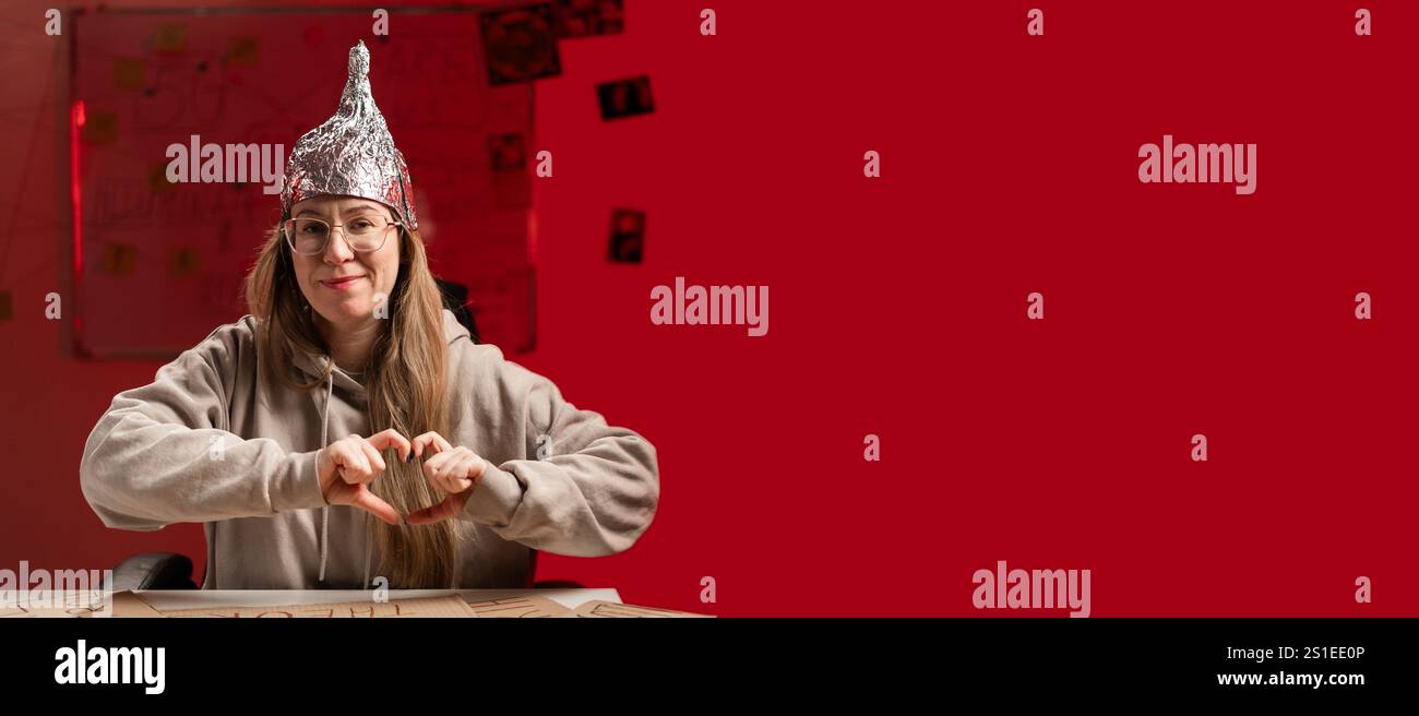 Woman wearing glasses in foil hat showing heart love gesture sitting on ...