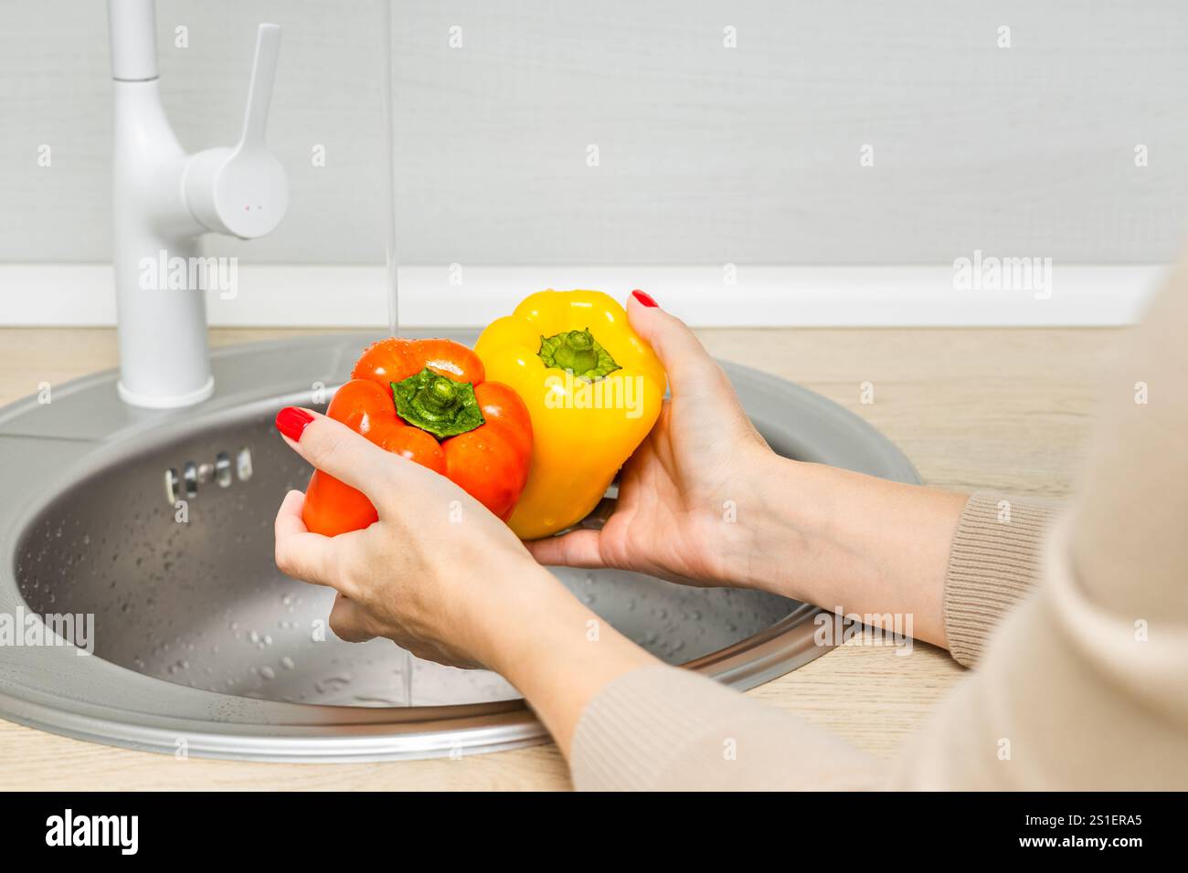 woman washing bell peppers in kitchen sink. housewife washes vegetables ...