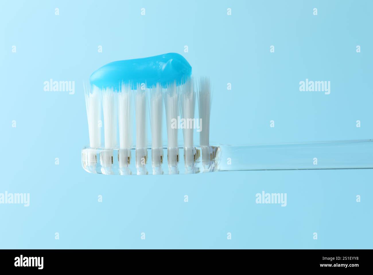 Toothbrush with toothpaste in air on light blue background, closeup ...