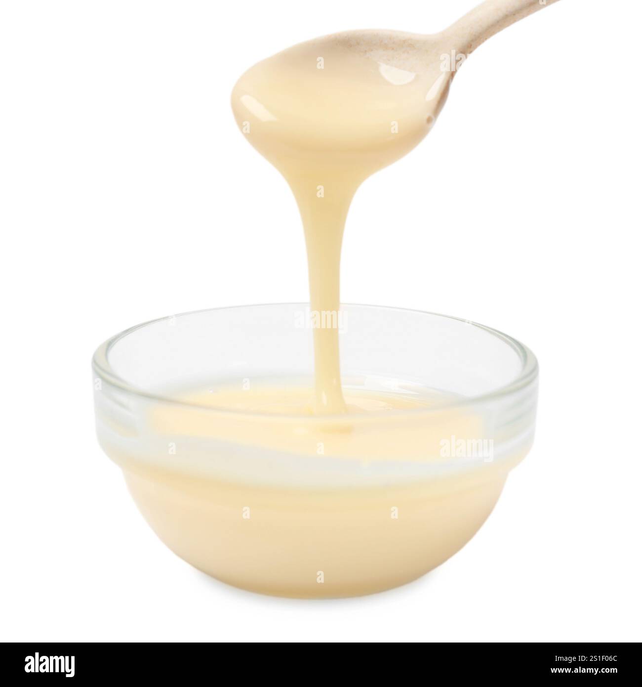 Condensed milk flowing down from spoon into bowl isolated on white ...