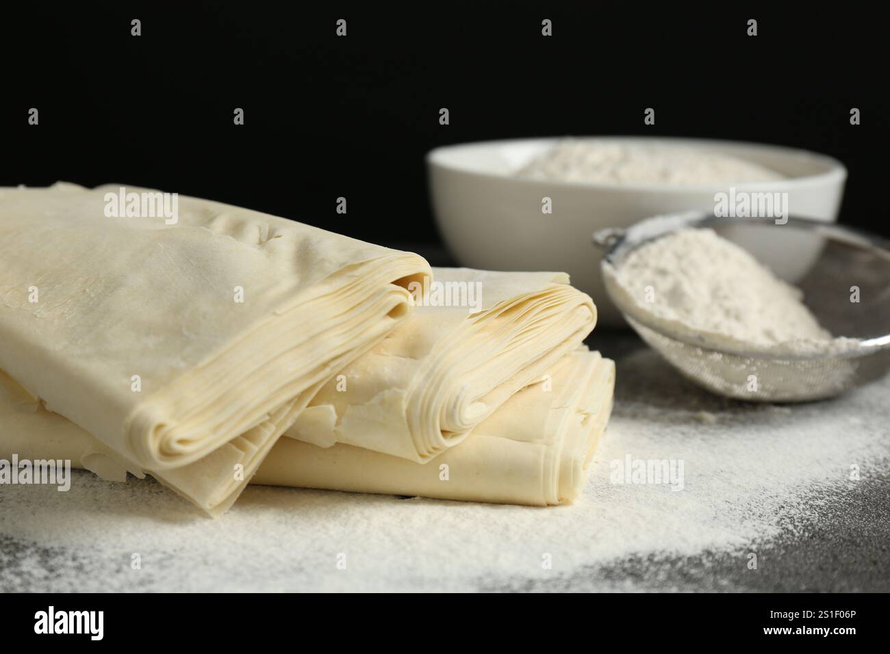 Raw puff pastry dough and flour on dark table against black background ...