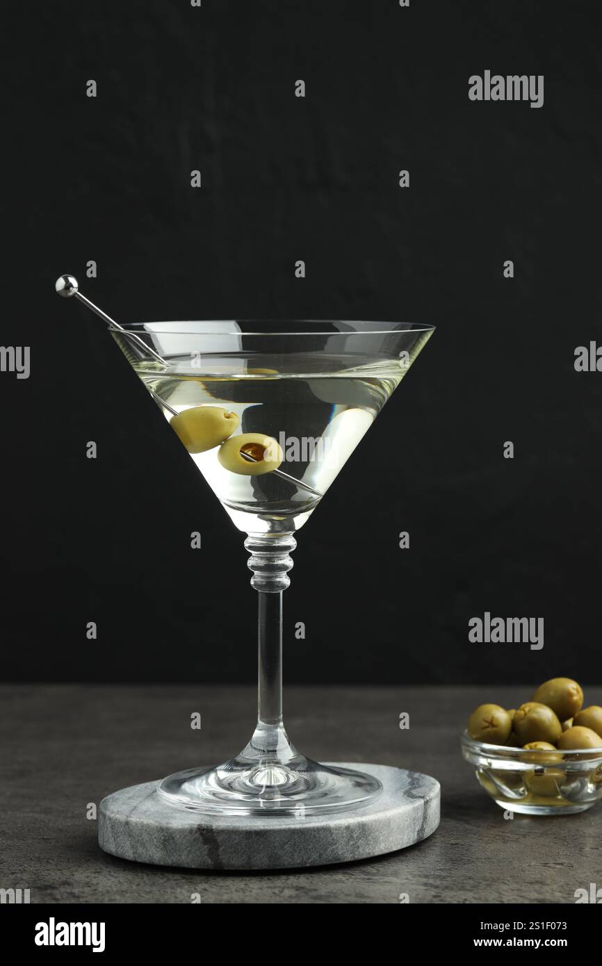 Martini cocktail with olives in glass on grey table against black ...